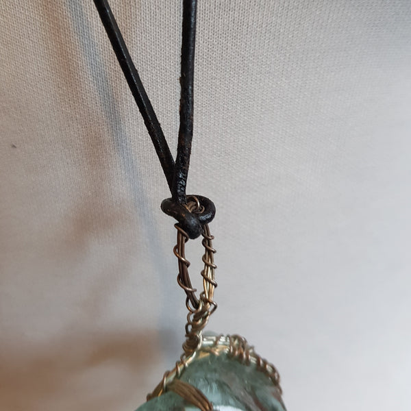 Transparent pendant in a metallic casing with a black leather cord, wi ...